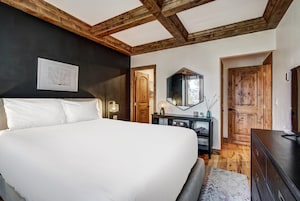 Um quarto com uma cama grande, teto de madeira, parede escura, um espelho e uma porta de madeira.