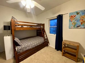 Quarto com beliche, ventilador de teto, janela com cortinas e um mapa na parede.
