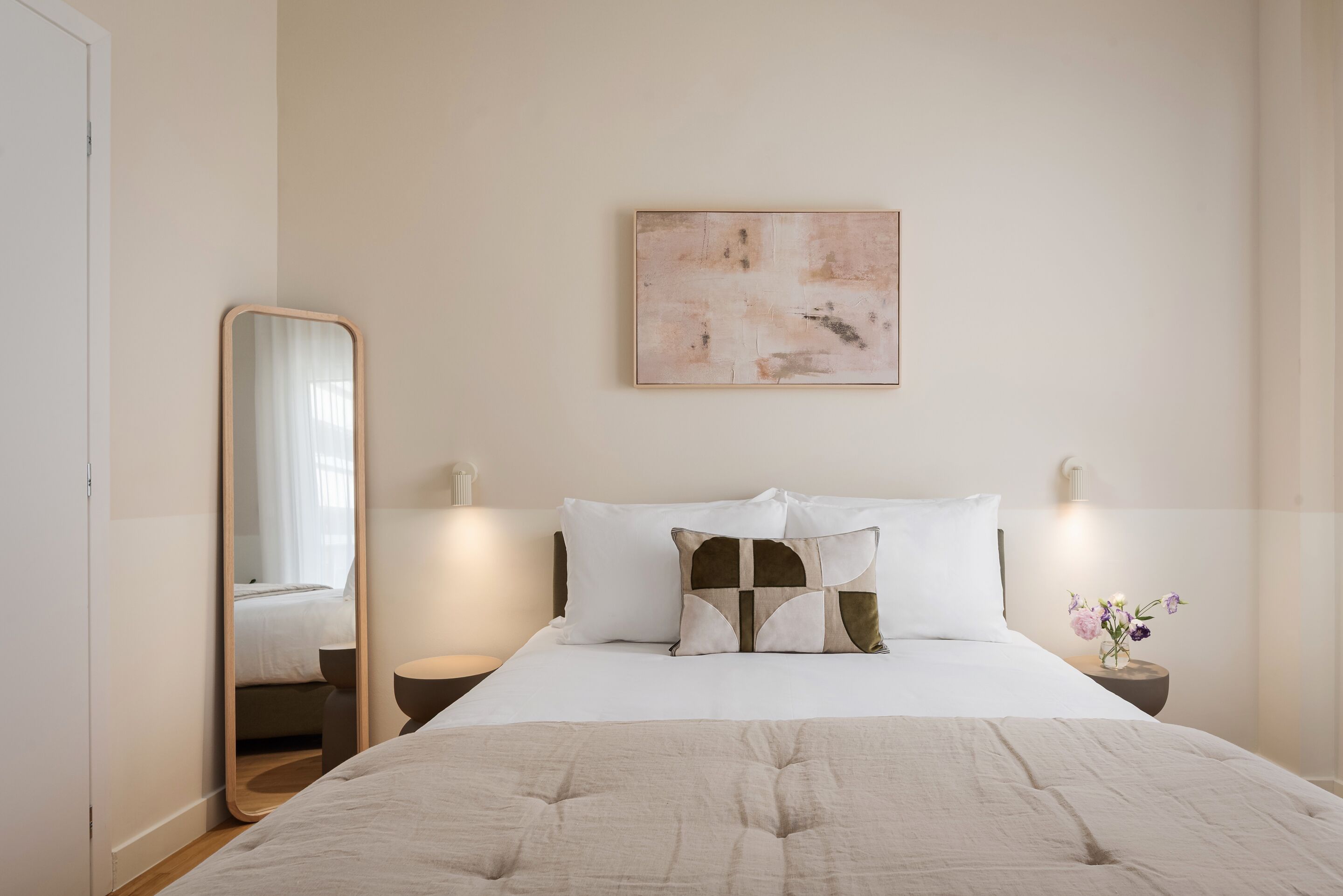 Um quarto com uma cama, uma mesa de cabeceira, um espelho e uma obra de arte na parede.