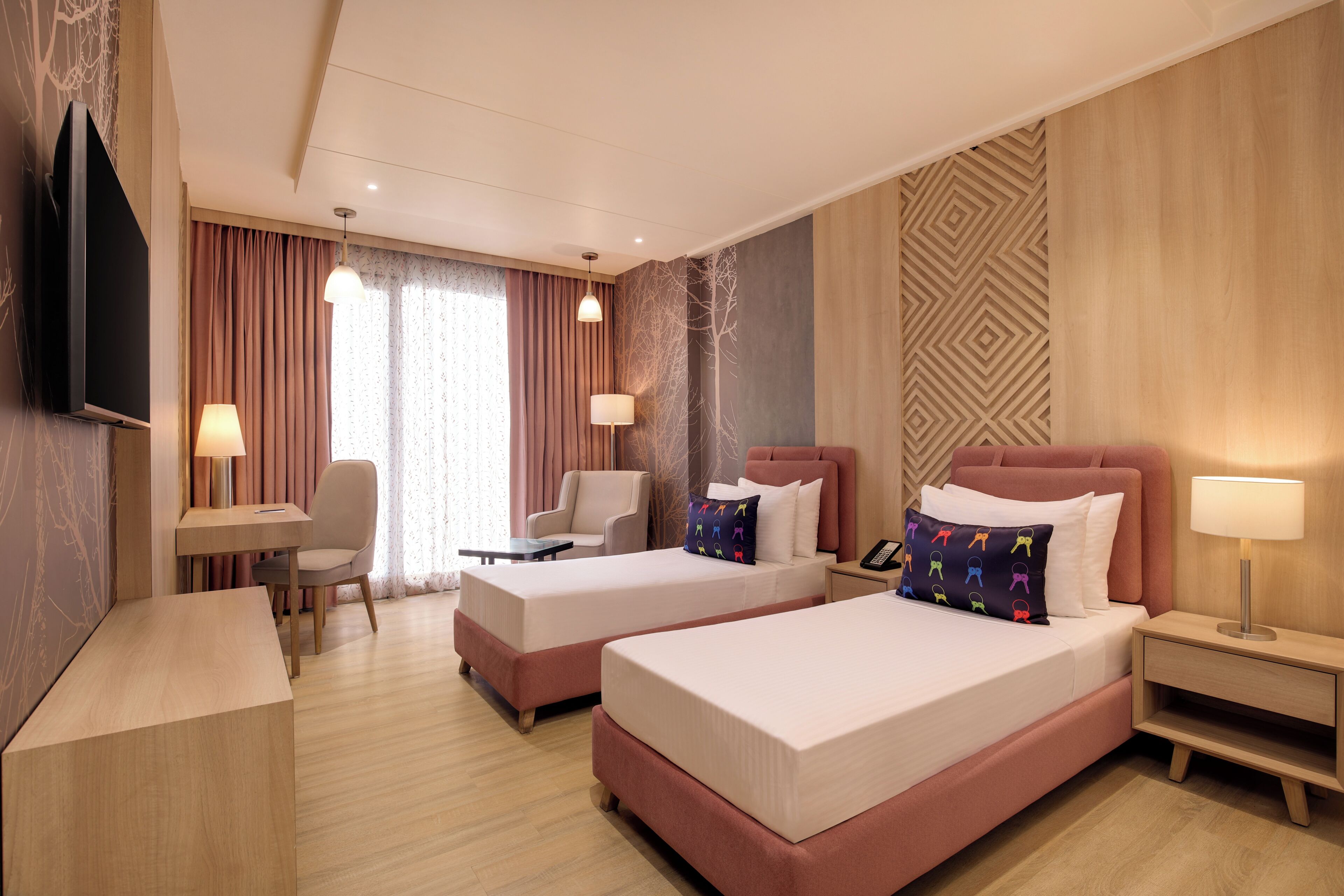 Quarto de hotel com duas camas, uma escrivaninha, uma cadeira, uma televisão e um abajur.