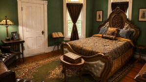 Quarto tradicional com uma cama grande, uma cadeira de madeira, uma mesinha e um abajur.
