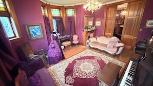 A room with a piano, a sofa, a patterned rug, and a mannequin in a dress.
