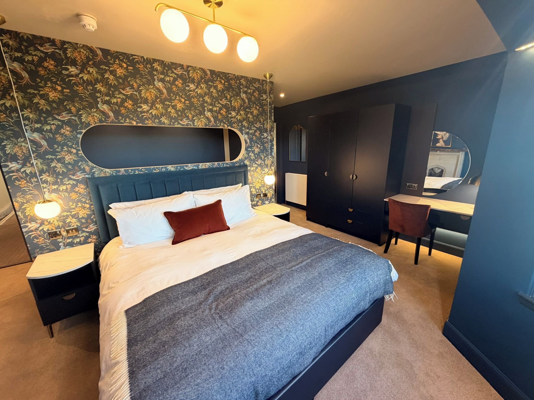 Quarto moderno com cama, mesas de cabeceira, cômoda e escrivaninha.