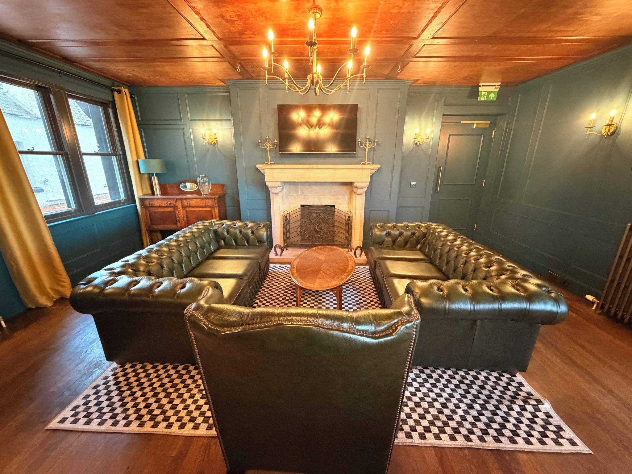 Quarto com lareira, sofás de couro, tapete xadrez e um candelabro.