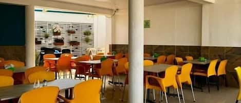 Uma cafeteria com mesas, cadeiras, um pilar e uma janela com persianas.