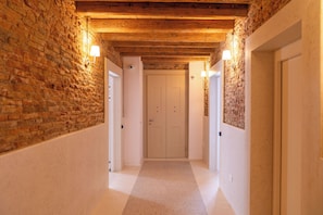 Corredor com vigas de madeira aparentes, paredes de tijolo e portas com luminárias.