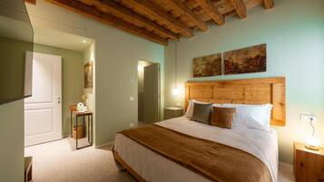 Quarto com cabeceira de madeira, cama com roupa de cama branca, mesa de cabeceira com abajur e um quadro na parede.