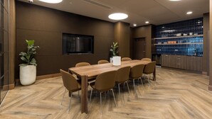 Uma sala de conferência com uma mesa de madeira, cadeiras marrons, uma televisão grande e uma copa com azulejos azuis.