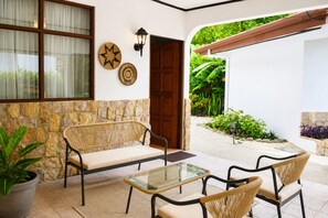 Um pátio com um sofá de vime, duas cadeiras, uma mesa de vidro e uma parede de pedra.