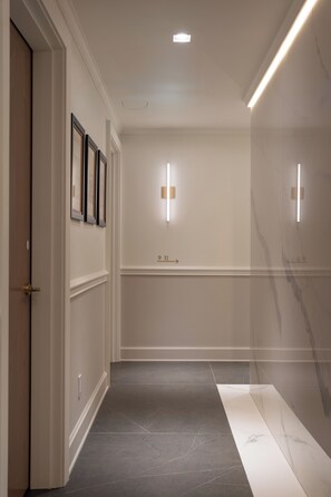 Um corredor com piso de mármore, quadros nas paredes e dois luminários fixados na parede.