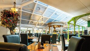 A spacious restaurant with high ceilings, a central dining area with tables and chairs, and a decorative hanging plant.