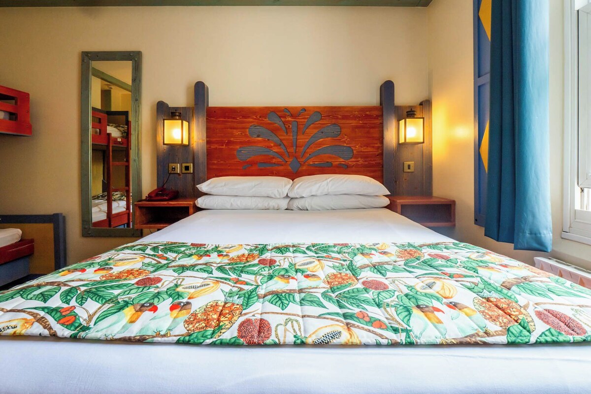 Quarto de hotel com uma cama grande, cabeceira de madeira, duas luminárias de cabeceira, mesa de cabeceira e um espelho.