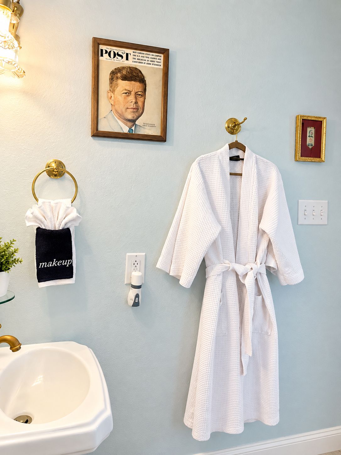 Casa de banho com pia branca, porta-toalhas com roupeiro, revista na parede e toalha de maquilhagem.