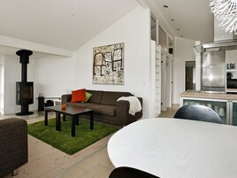 Uma sala de estar moderna com lareira, um espaço de jantar e uma cozinha com geladeira de aço inoxidável.