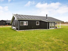 Um edifício moderno preto com telhado inclinado e chaminé, cercado por um campo gramado.