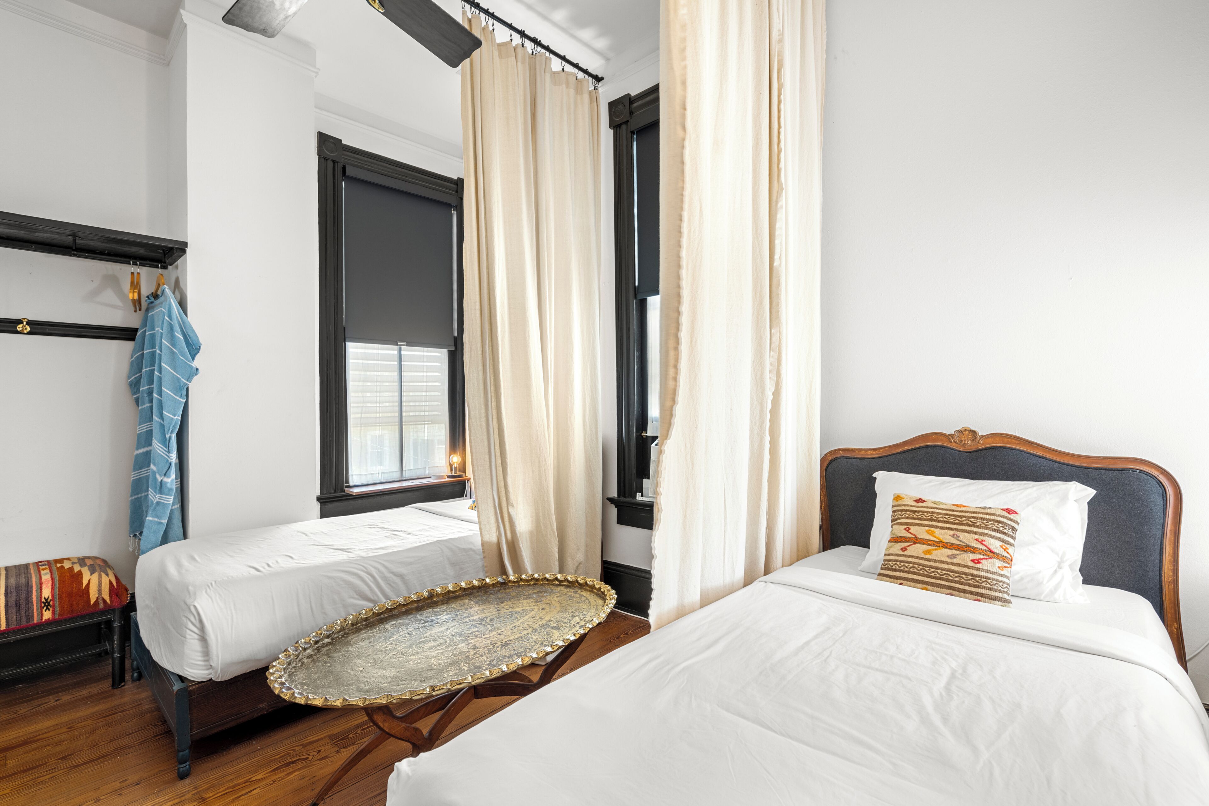 Quarto de hotel com duas camas, uma mesinha e uma janela com cortinas.