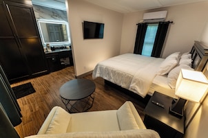 Quarto de hotel com cama, mesa de cabeceira, luminária e uma pequena mesa redonda.