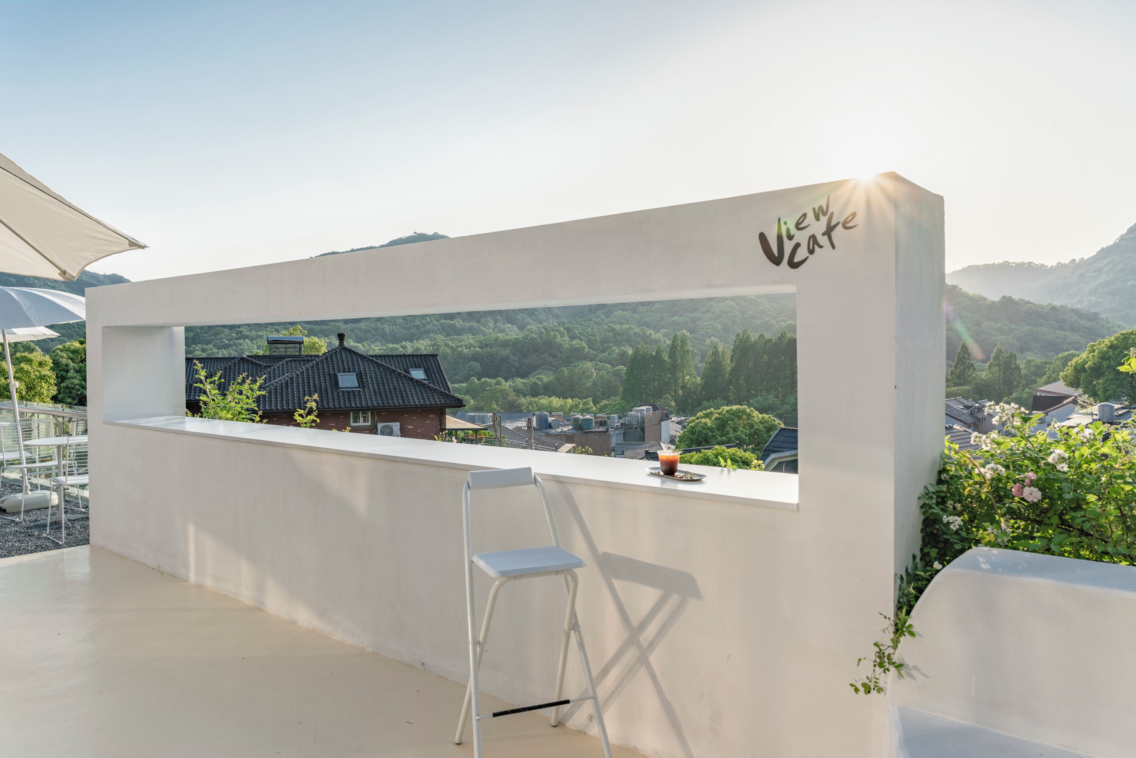 Uma área de estar externa branca com vista para uma casa e montanhas.