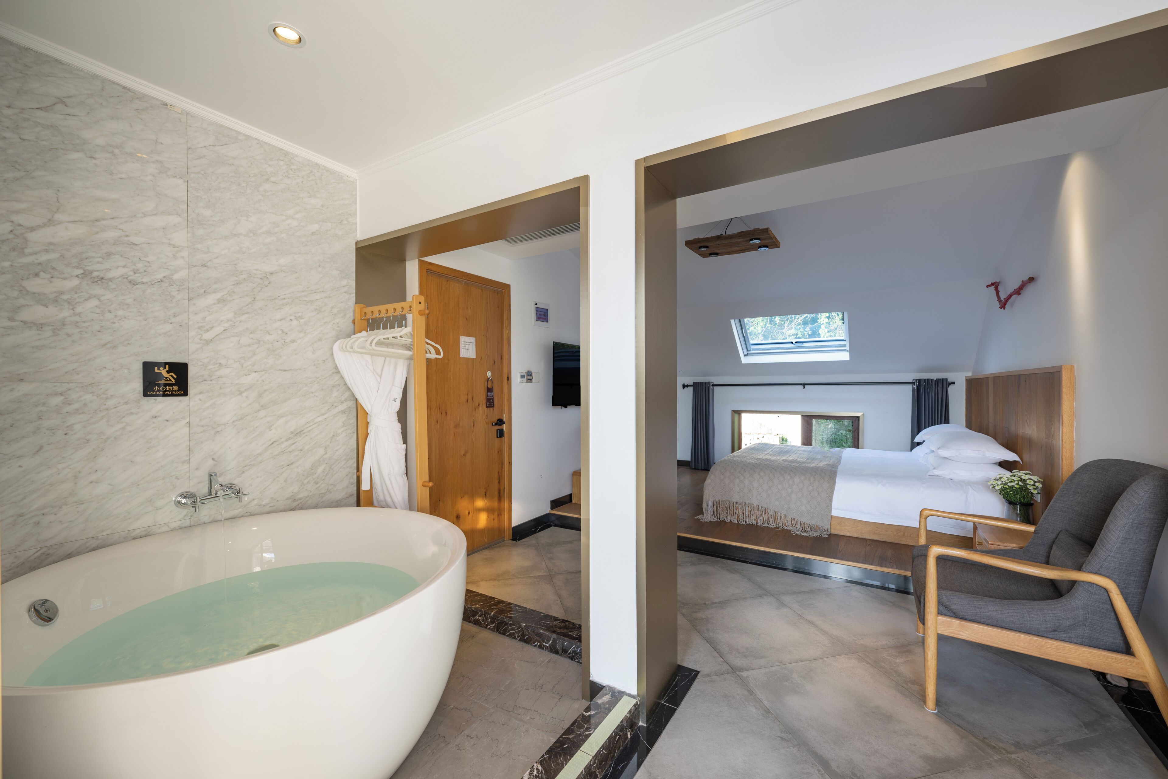 Um banheiro moderno com uma banheira separada e um quarto com cama e poltrona.