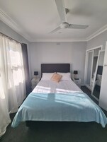 Um quarto com cama, ventilador de teto, mesa de cabeceira com abajur e guarda-roupa.