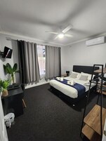 Quarto de hotel com cama, escrivaninha, cadeira e ventoinha no teto.