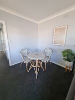 Quarto de canto com uma mesa de jantar e cadeiras, um vaso de planta e um quadro na parede.