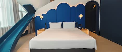 Quarto de hotel moderno com uma cama grande, uma mesa de cabeceira, um telefone fixado na parede e um painel de controle.