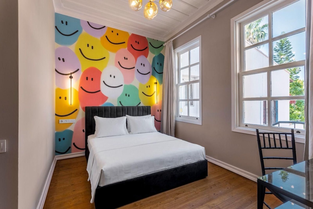 Quarto com cama, janela e parede decorada com carinhas sorridentes.
