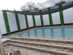 Piscina com degraus de acesso, rodeada por paredes brancas com detalhes verticais verdes.
