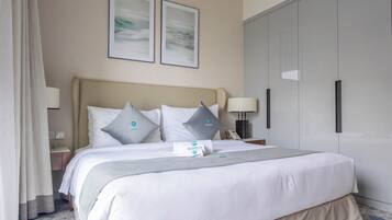 Quarto de hotel com cama, mesa de cabeceira, abajur, guarda-roupa e duas imagens emolduradas na parede.