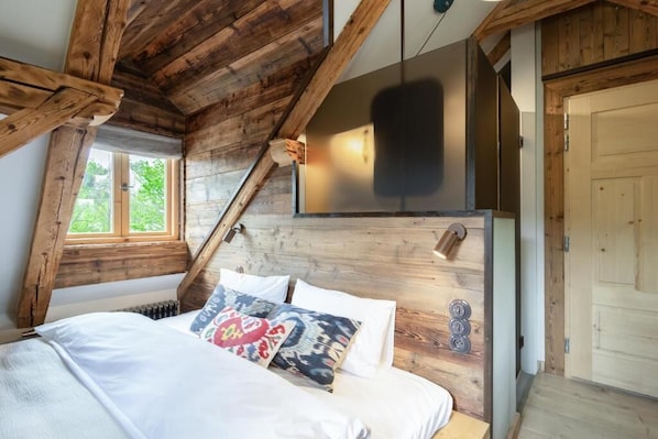 Um quarto com teto inclinado, uma cama com almofadas estampadas, uma janela e uma porta.