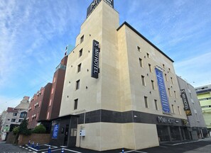 Um edifício de hotel com vários andares e uma placa grande com a inscrição 'MH HOTEL' na fachada.