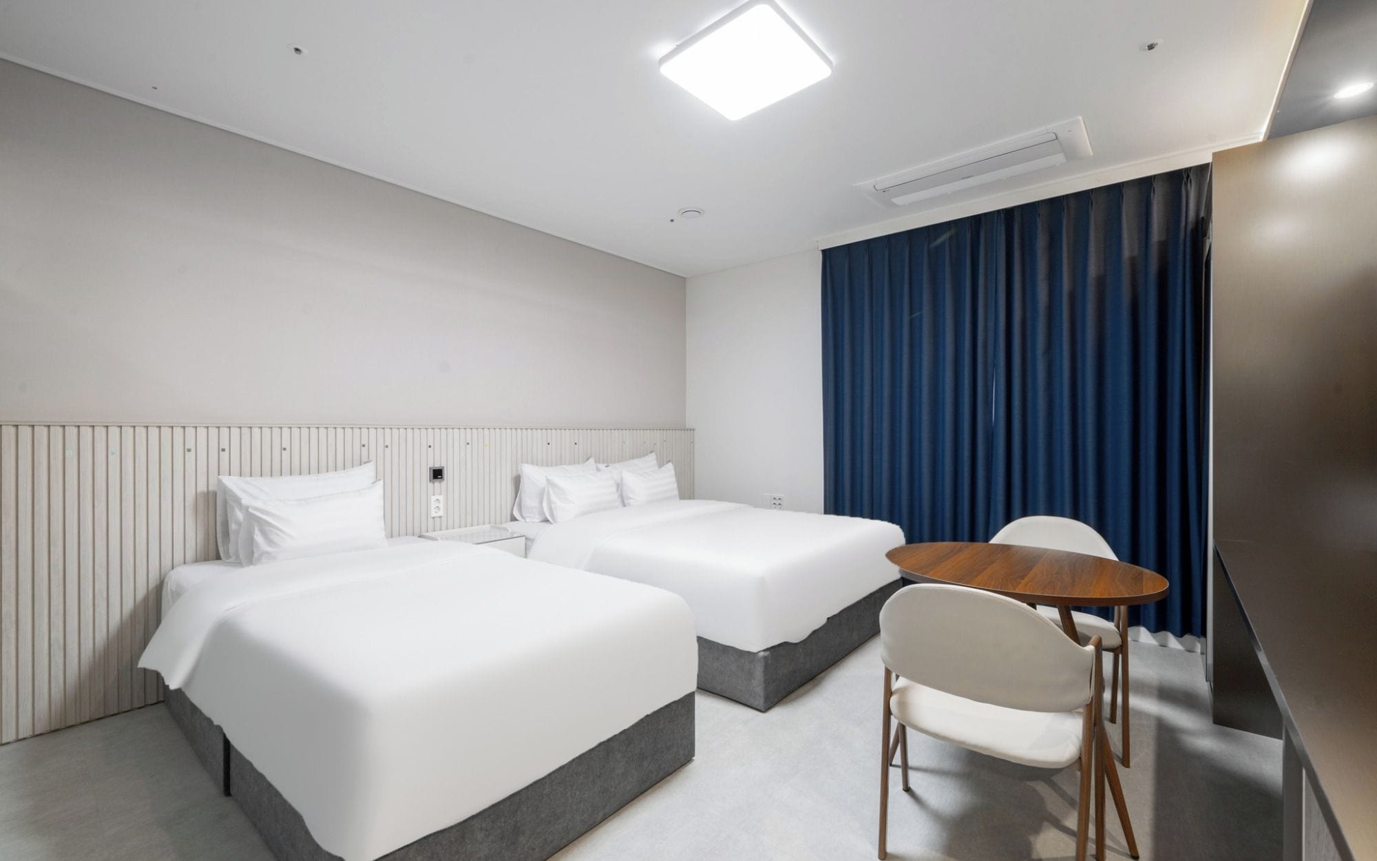 Quarto de hotel com duas camas, uma mesinha e uma cadeira.