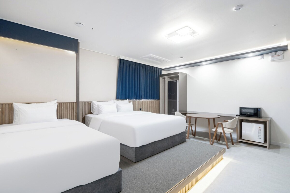 Quarto de hotel com duas camas, uma escrivaninha, micro-ondas e um pequeno espaço de estar.