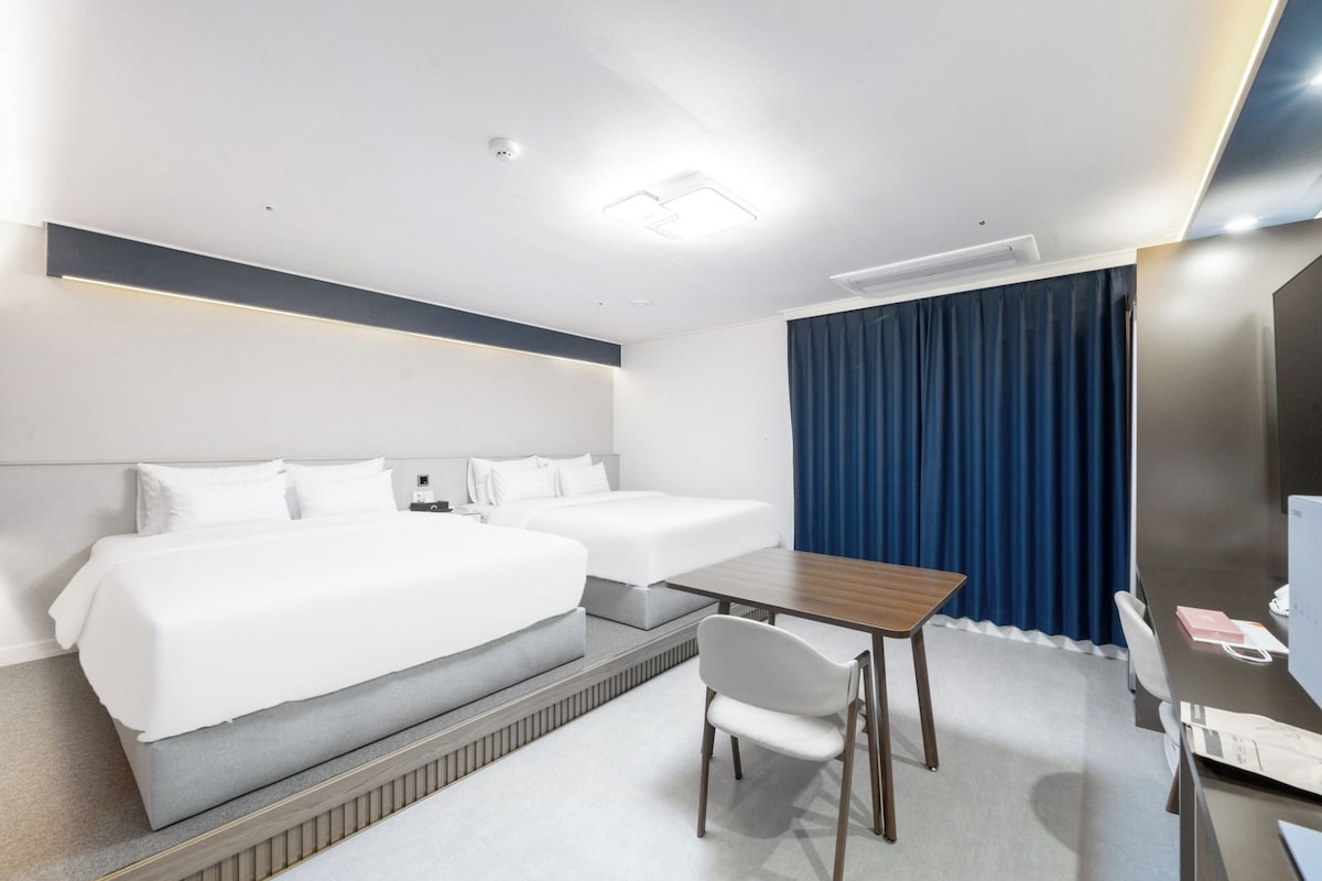 Quarto de hotel com cama, mesas de cabeceira, escrivaninha e uma cadeira.