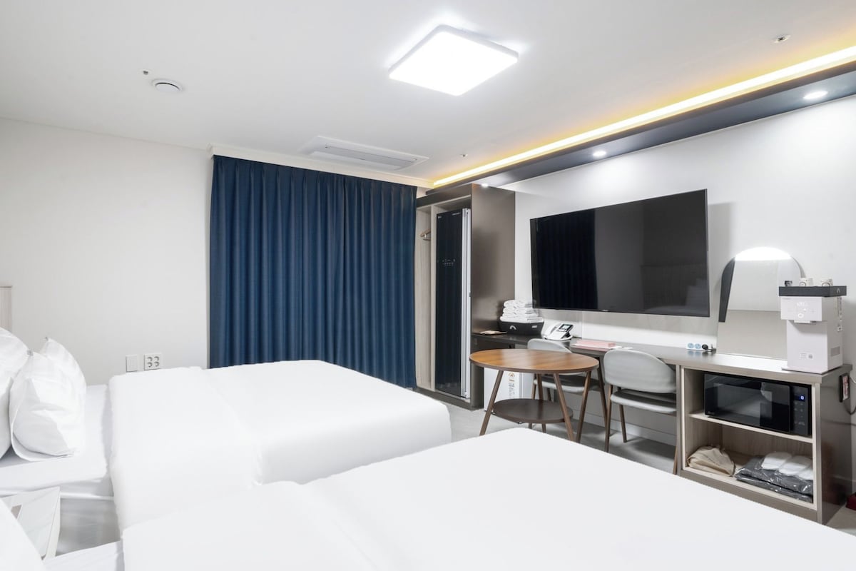 Quarto de hotel com duas camas, uma escrivaninha, televisão de tela plana e minibar.