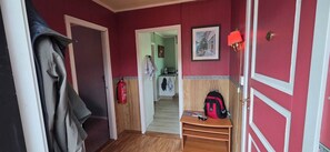 Um corredor com um cabideiro, um extintor de incêndio, uma mesa com uma mochila e um quadro na parede.