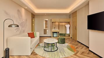 Quarto de hotel moderno com sofá, mesa de centro redonda, televisão e guarda-roupa.