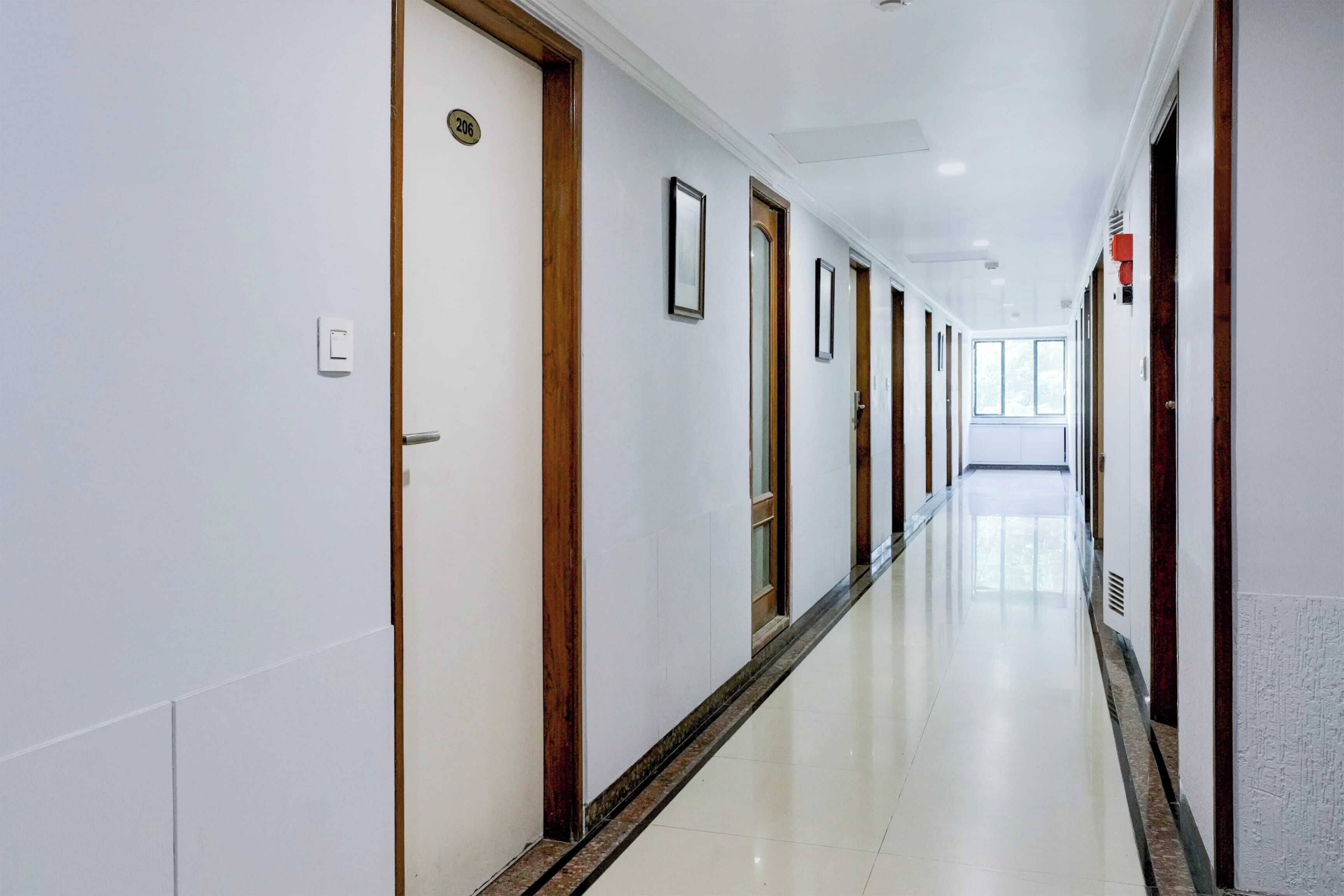 Um corredor longo e bem iluminado, com portas, um interruptor de luz e um número na parede.