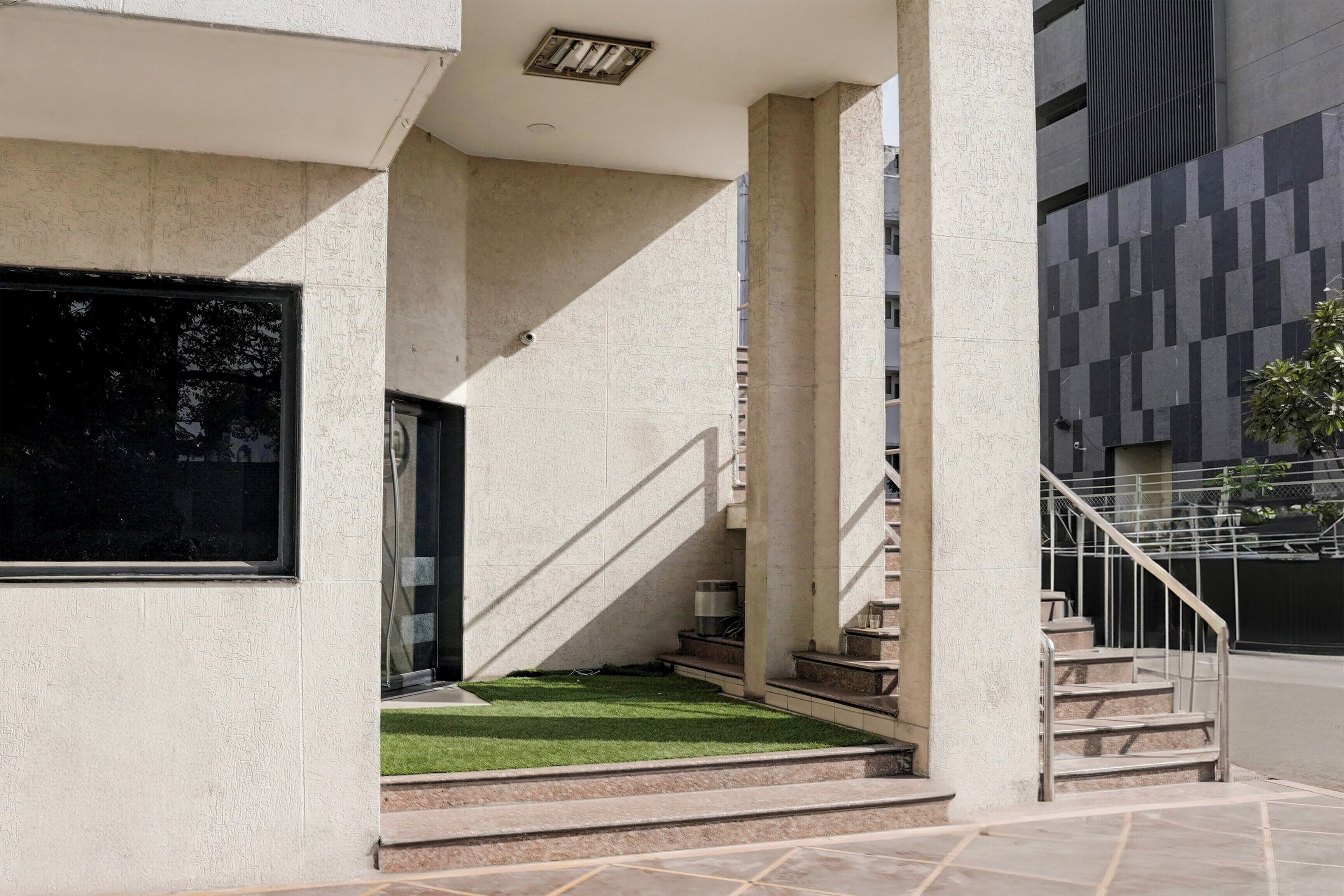 Entrada de um edifício com uma escadaria que desce para um nível inferior, uma janela com moldura preta e corrimão de metal na escada.