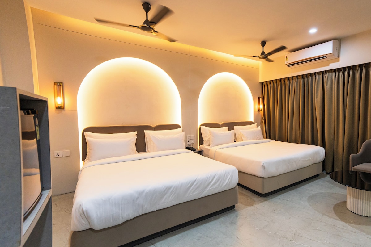 Quarto de hotel com duas camas, uma cadeira, ar-condicionado e ventilador de teto.
