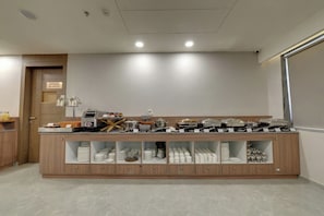Buffet montado com diversos pratos e utensílios, placa indicando entrada proibida na cozinha e um armário de madeira com espaço de armazenamento embaixo.