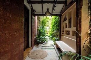 Corredor estreito com porta de madeira, parede de pedra, luminária pendente e parede coberta de plantas verdes.