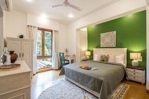 Quarto com cama, mesas de cabeceira, escrivaninha, janela com cortinas e uma parede verde como detalhe.