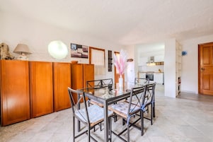 Uma área de refeições com mesa de vidro, cadeiras de madeira e um vaso com penas.