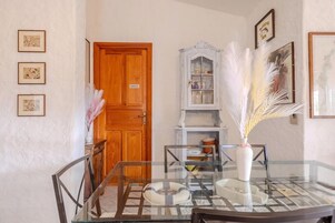 Uma sala de jantar com mesa de vidro, cadeiras, porta de madeira e um armário branco com portas de vidro.
