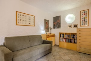 Uma sala de estar com um sofá, uma escrivaninha de madeira, uma estante de livros e várias imagens emolduradas nas paredes.