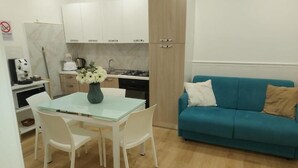 Uma cozinha compacta com armários brancos, uma mesa de jantar com cadeiras e um sofá verde-água com almofadas.