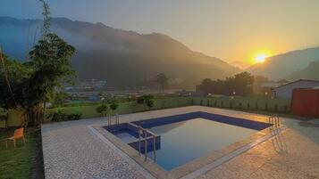 Uma piscina retangular com deck ladrilhado, rodeada por um muro baixo e área gramada.
