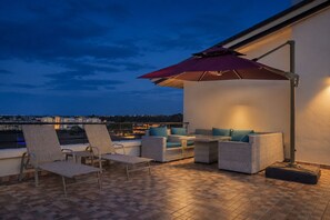 Terraço no telhado com área de estar ao ar livre, vista para o horizonte urbano e um grande guarda-sol para proteção contra o sol.
